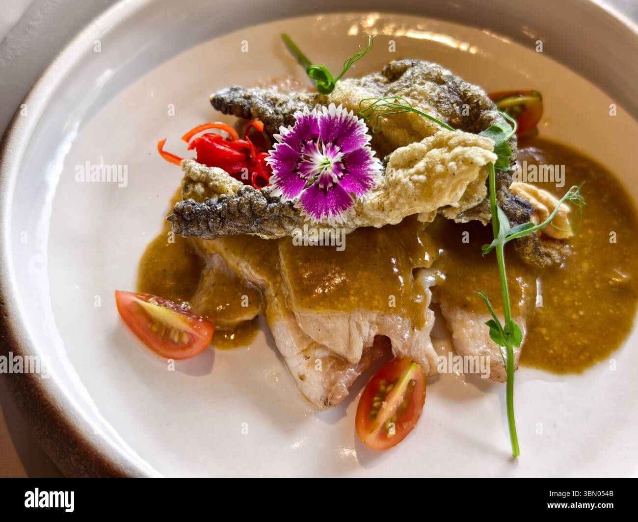 A fillet of fish topped with crispy skin, curry sauce, cherry tomatoes ...