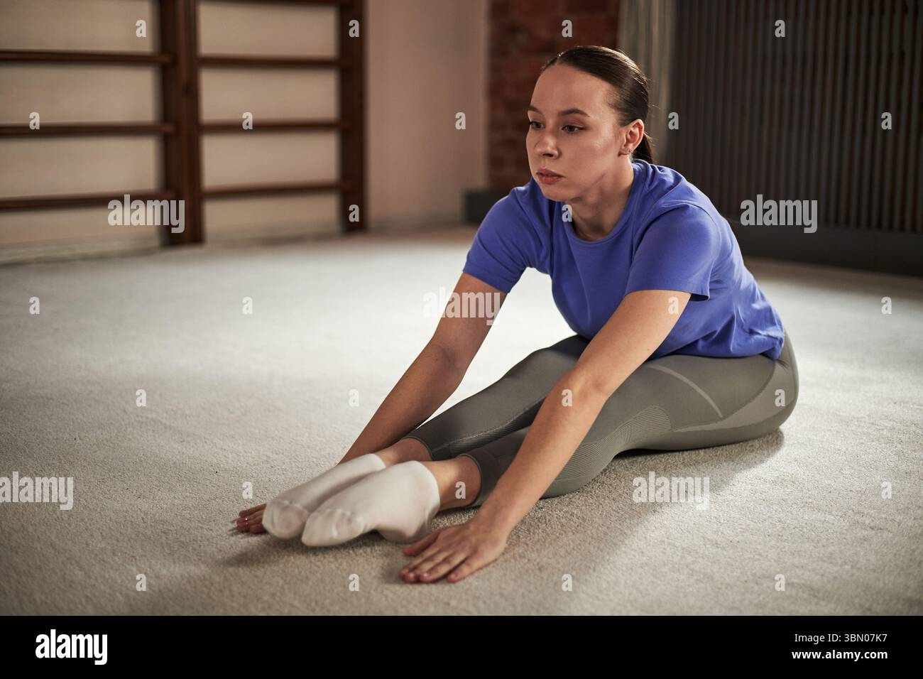 Caucasian young adult woman sitting on floor stretching legs forward ...