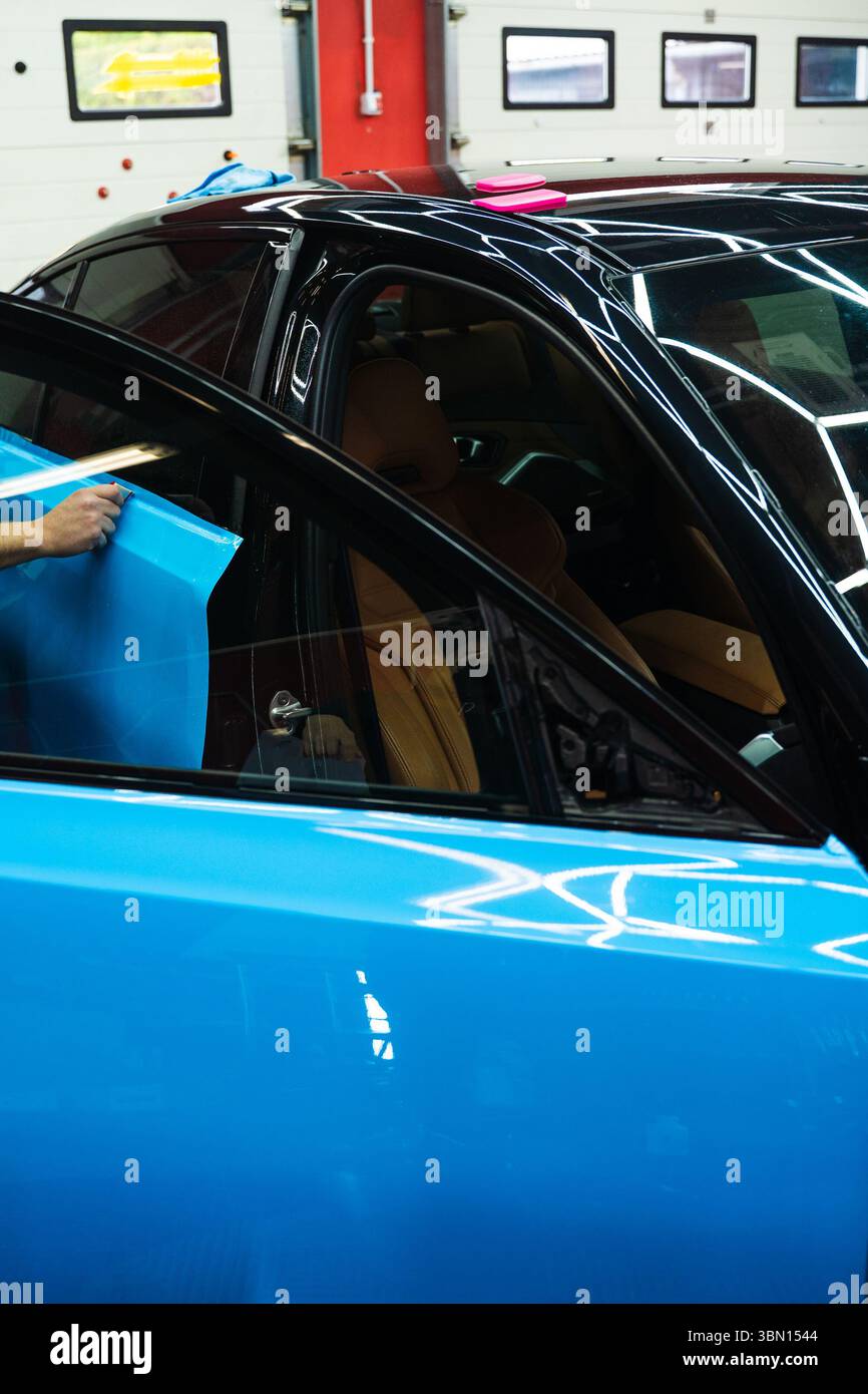 Detailing expert uses red squeegee wrapper to flatten blue PPF wrap on ...