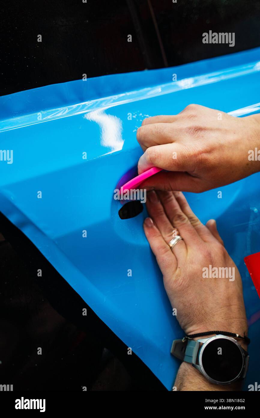 Detailing expert uses red squeegee wrapper to flatten blue PPF wrap on ...
