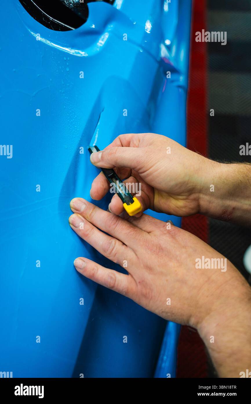 Detailing technician trims blue PPF on a car panel for perfect contour ...