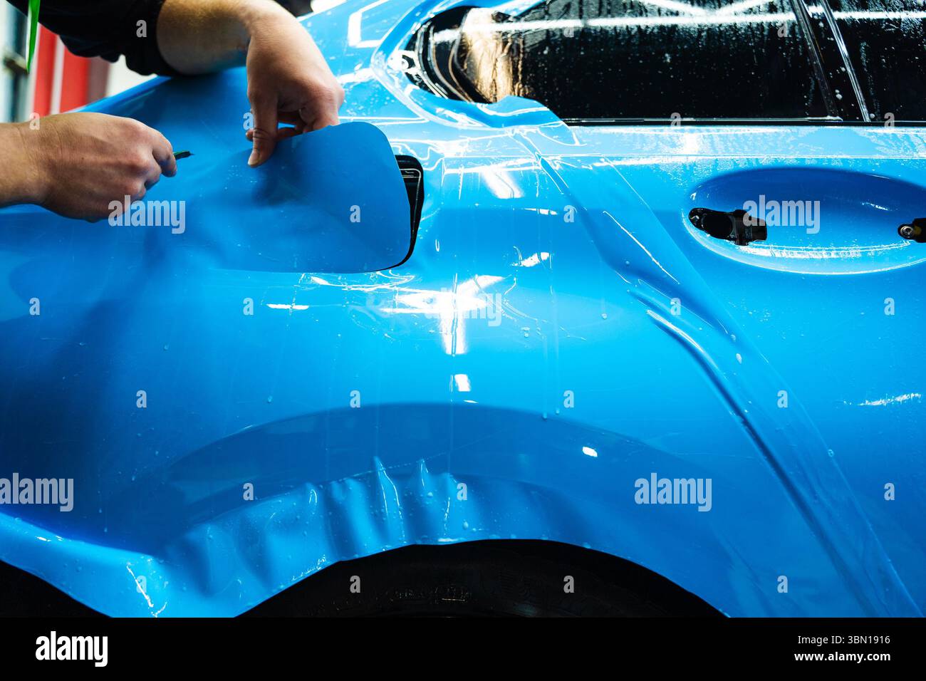 Detailing technician trims blue PPF on a car panel for perfect contour ...