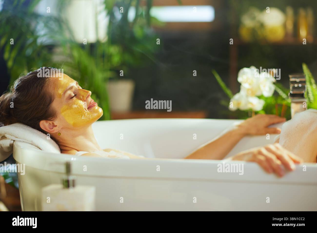 Woman with brown hair, eyes closed & yellow facial mask relaxes in ...