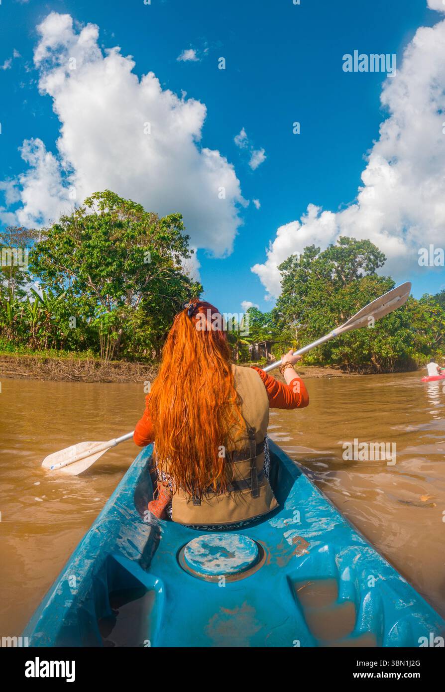 A picturesque view of a woman kayaking in the Amazon rainforest, surrounded by lush greenery and ...