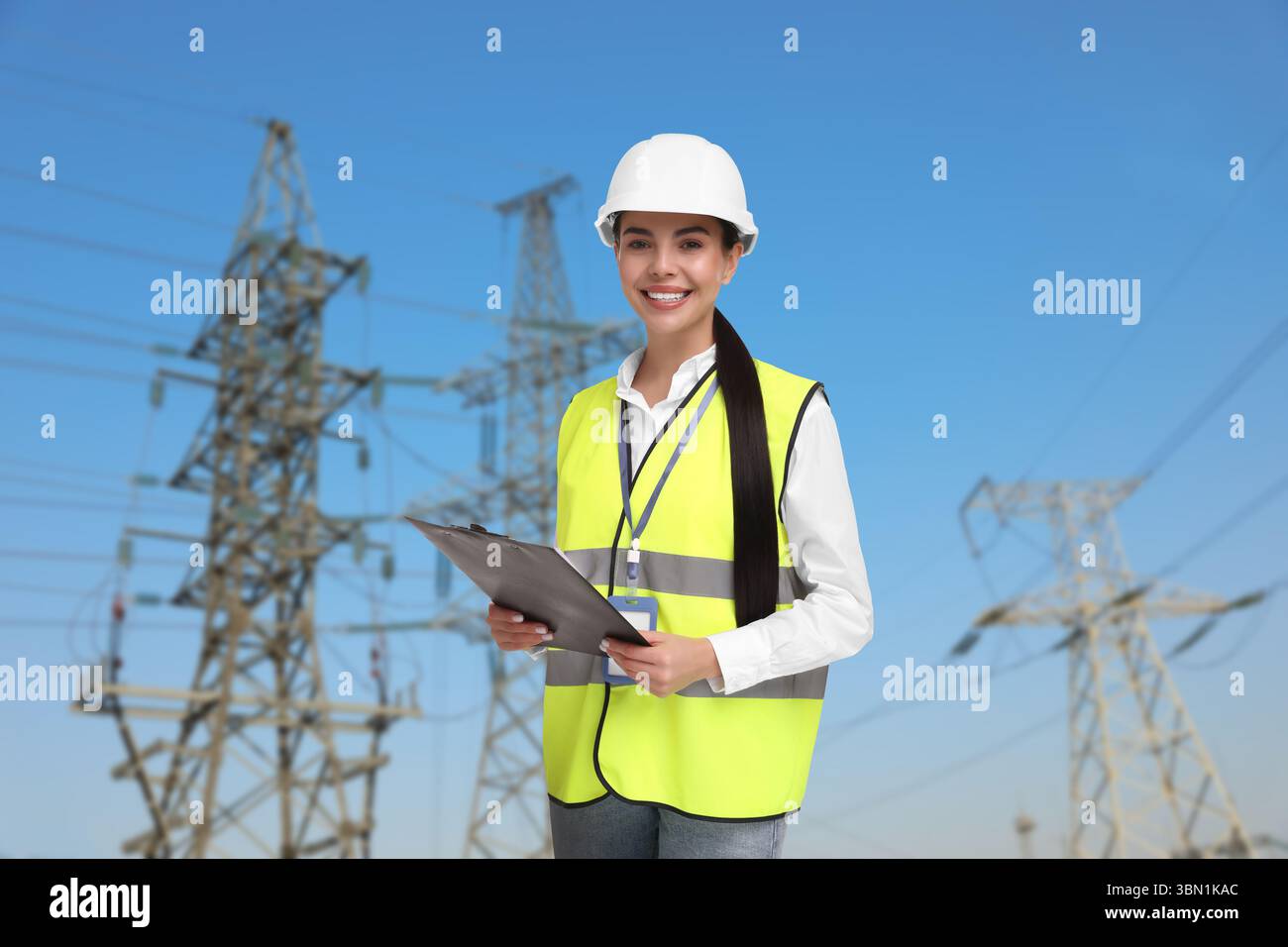 Power engineer in hard hat holding clipboard against high voltage ...