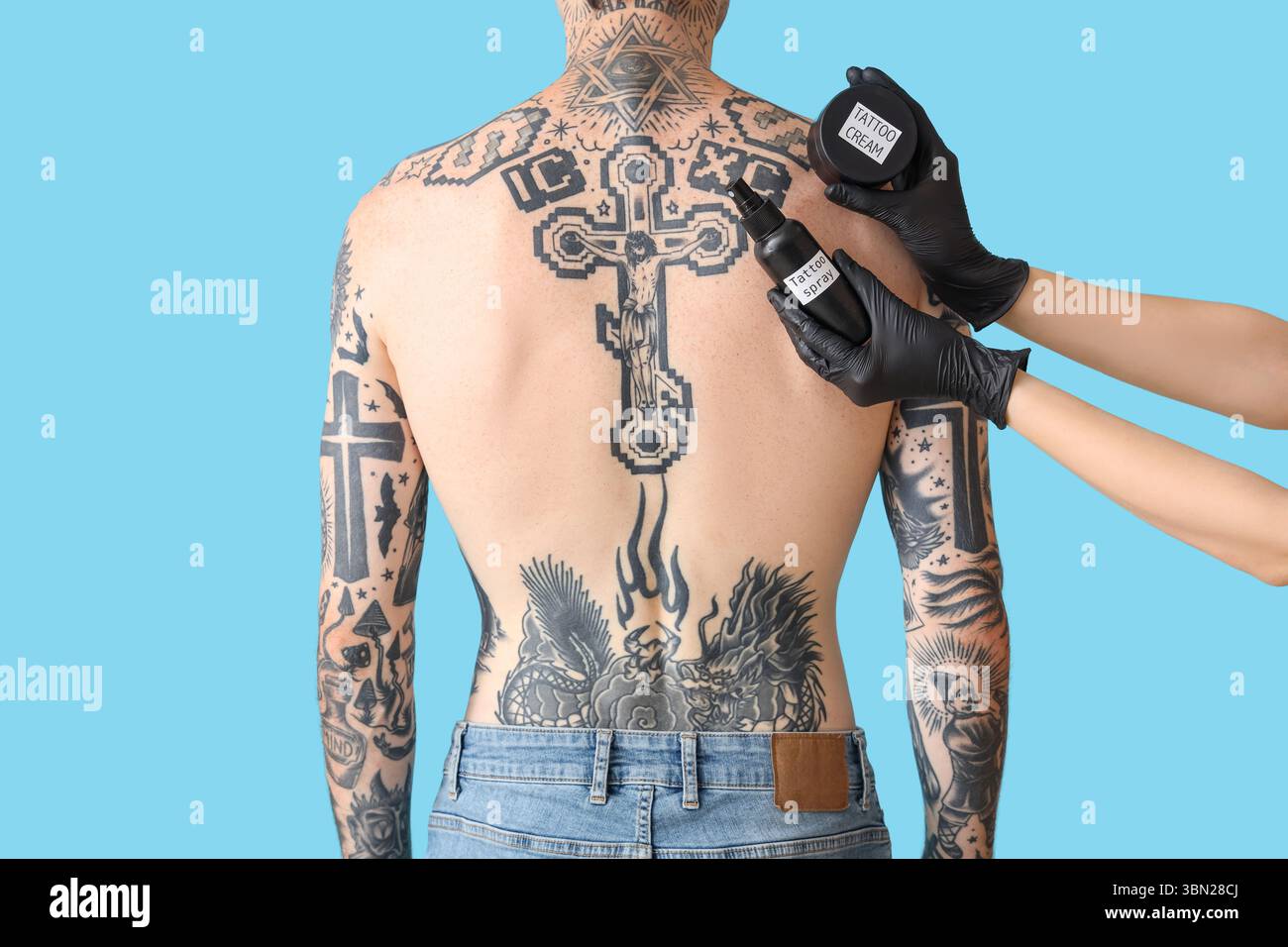 Tattoo master in gloves holding tattoo spray and cream near tattooed ...