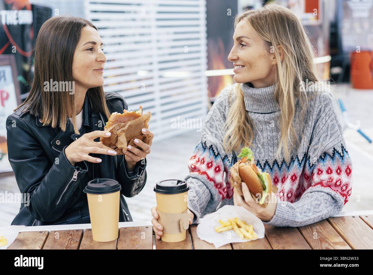 Zwei Frauen mittleren Alters essen Burger auf einem Street Food Truck ...