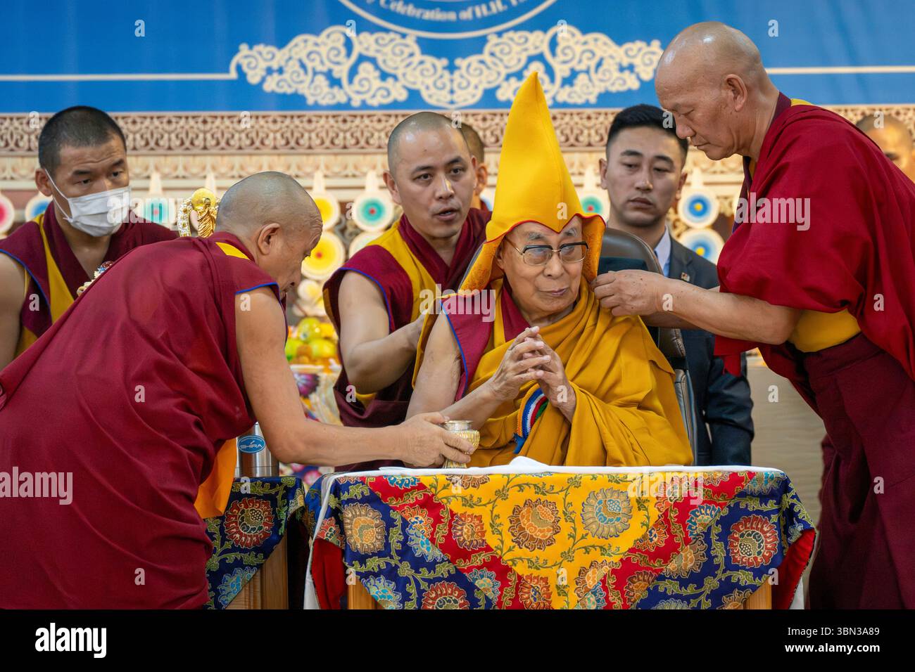 Attendant monks help Tibetan spiritual leader the Dalai Lama wear a ...
