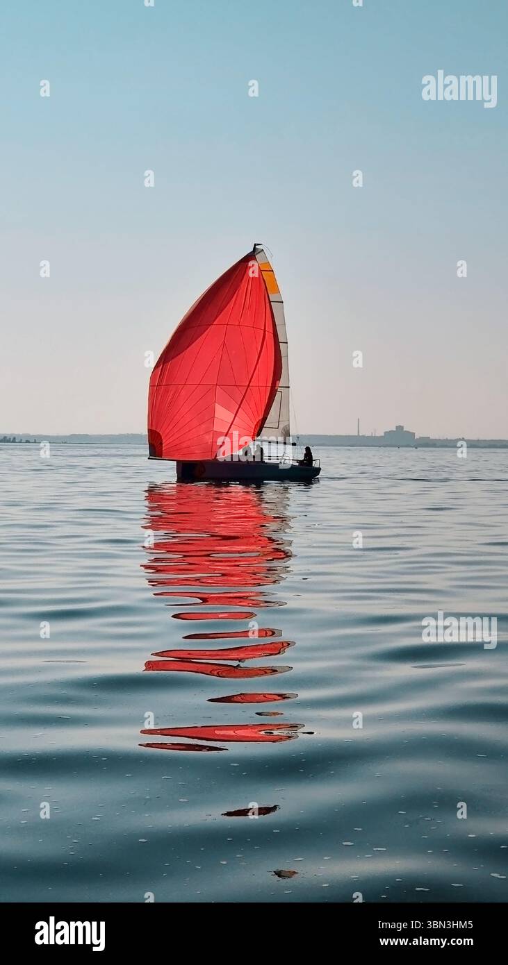 A sailboat with a vibrant red spinnaker sail glides smoothly across ...