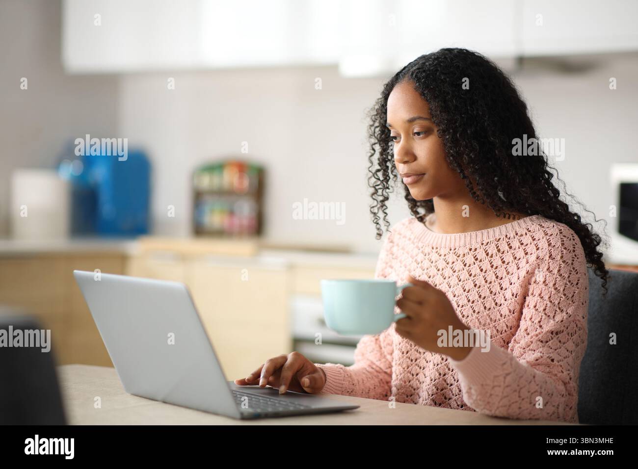 Serious black woman drinking coffee and checking computer in a kitchen at home Stock Photo - Alamy