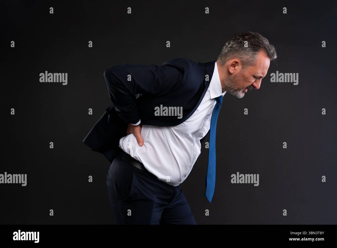 Mature man in a suit holding his lower back in pain, bending forward and grimacing, indicating ...