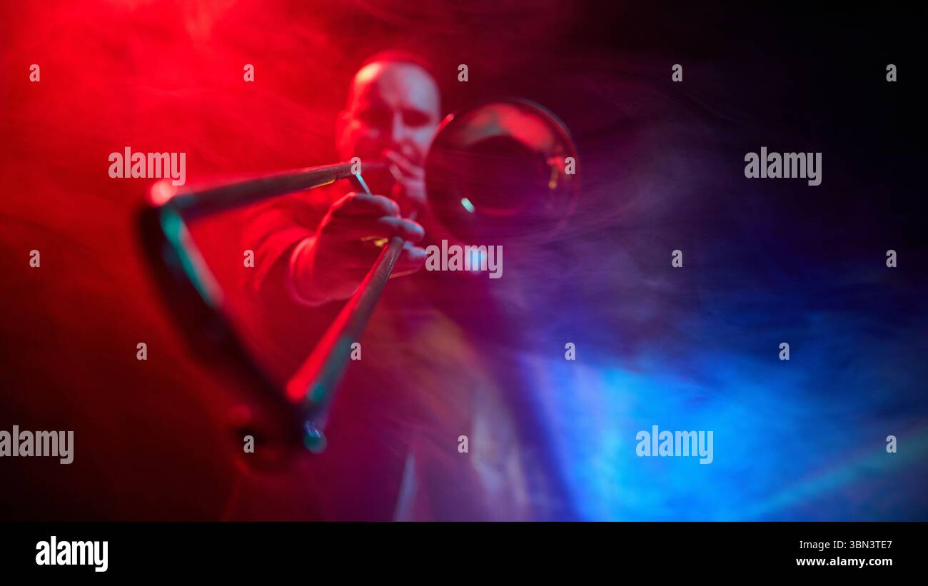 Musician playing trombone on stage with dramatic red and blue lighting ...