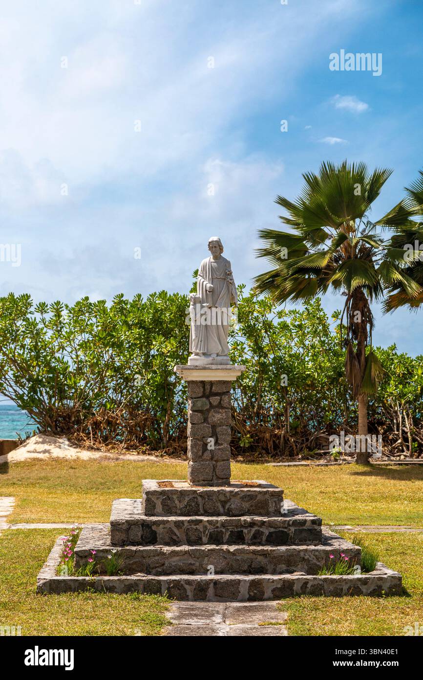 A stone monument stands on a grassy area with palm trees and blue sky ...
