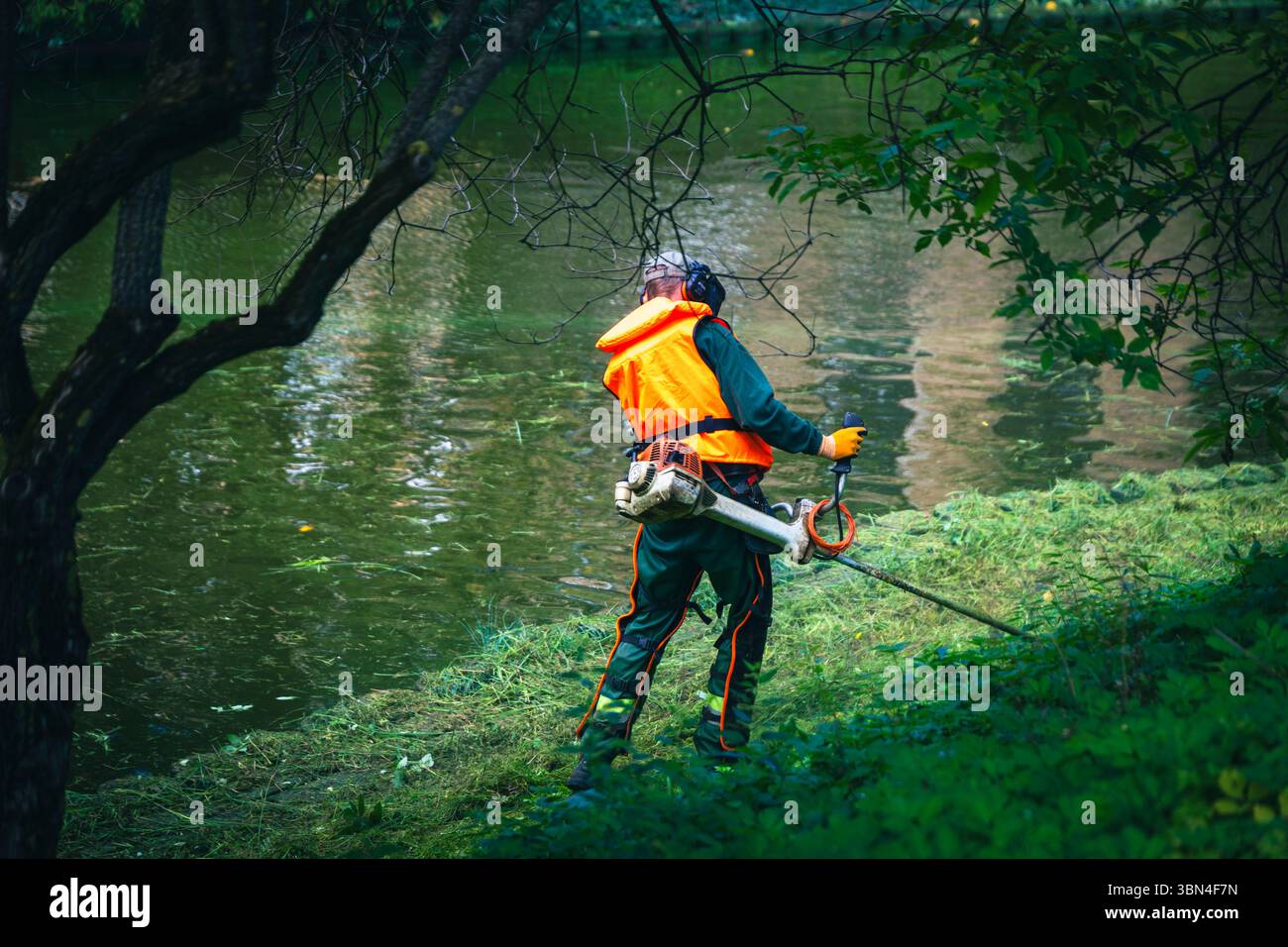 Worker with brushcutter and lifejacket for work near water Stock Photo ...