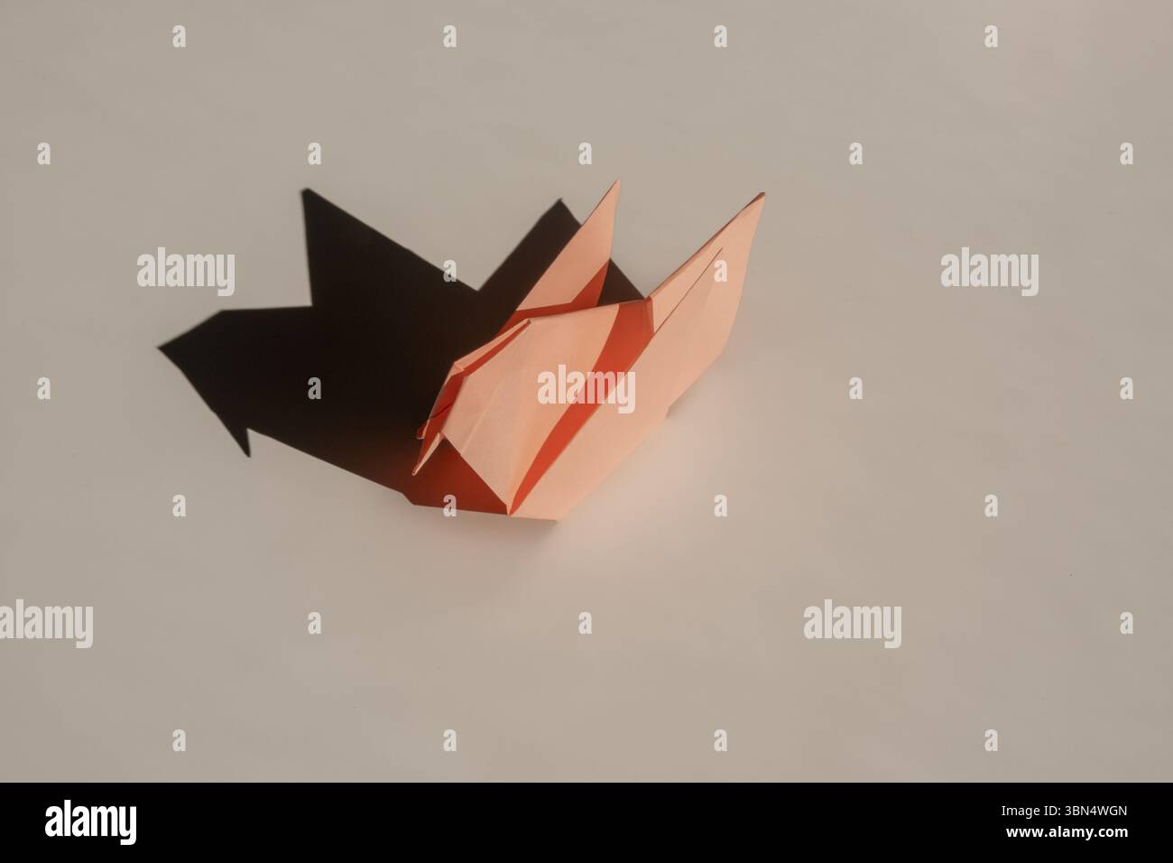 Minimalistic photo of a peach paper bird figure casting a sharp shadow ...