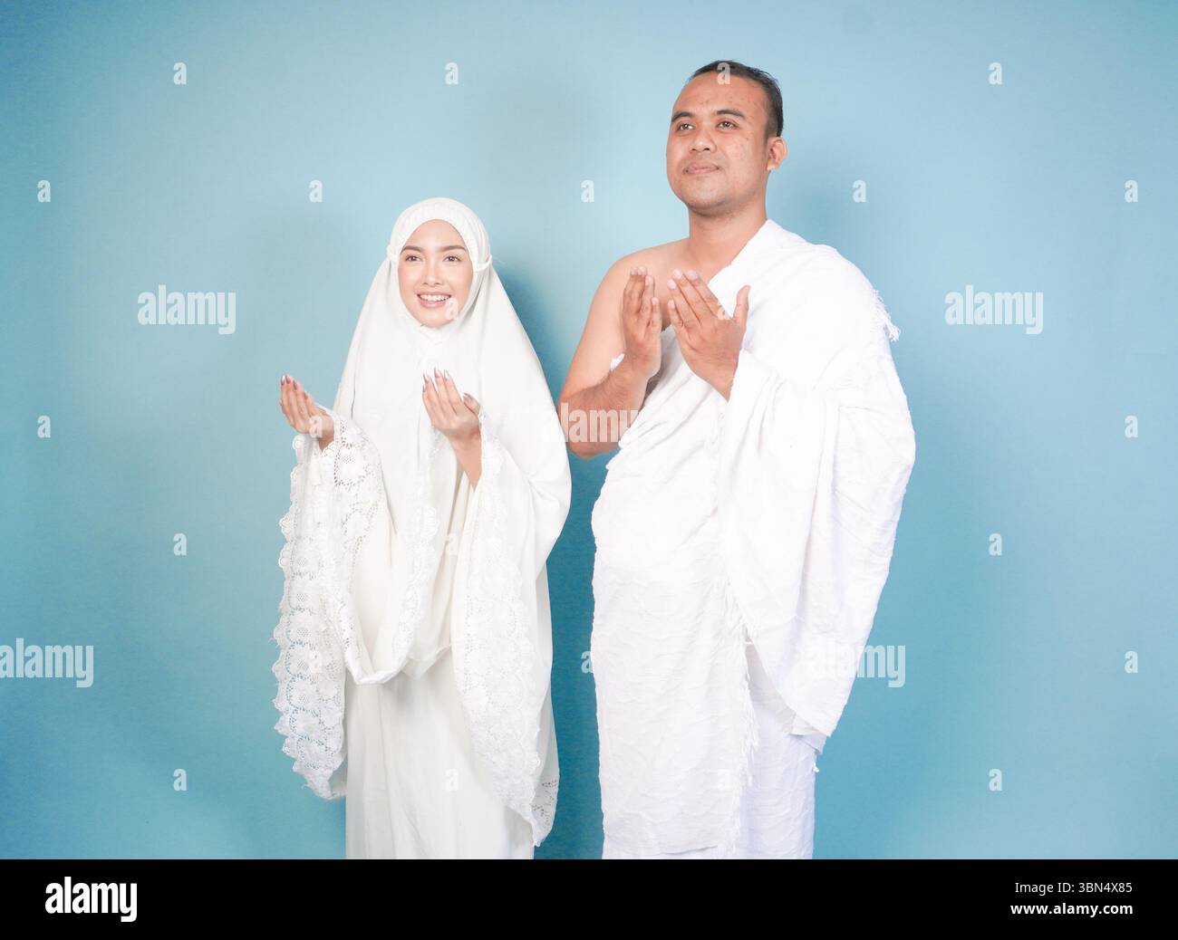 young Asian Muslim couple wearing ihram and prayer gown doing praying ...