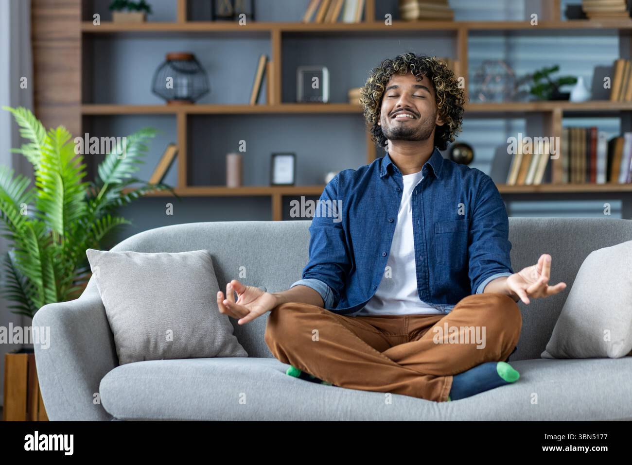 A man meditates peacefully at home, sitting comfortably on a sofa with ...
