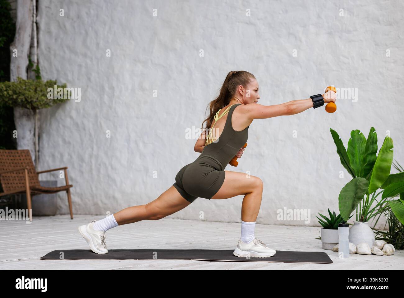 Young woman training with dumbbells in a lunge position at home modern ...