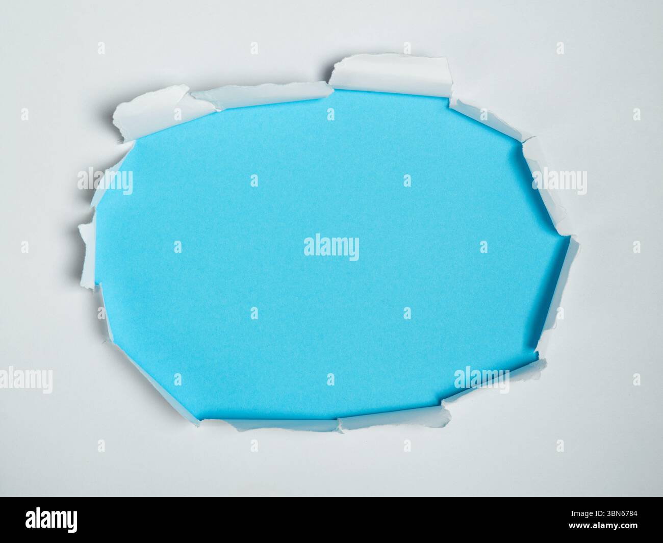 Tear hole in center of white paper reveals light blue background Stock ...