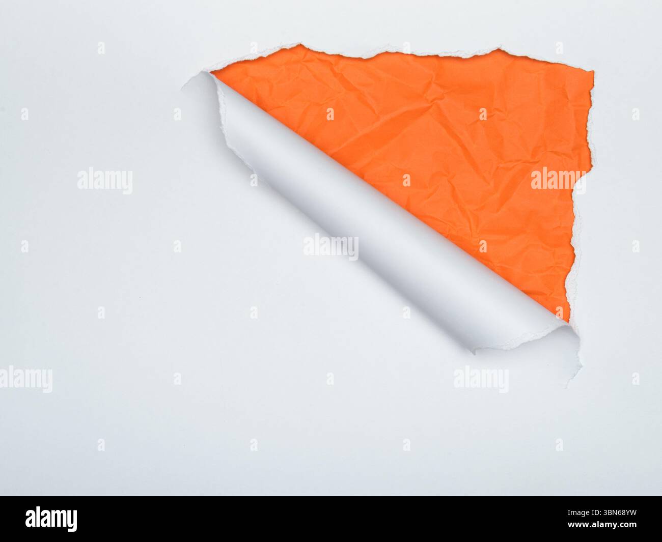 A piece of white paper is torn, revealing a vibrant orange, crumpled ...