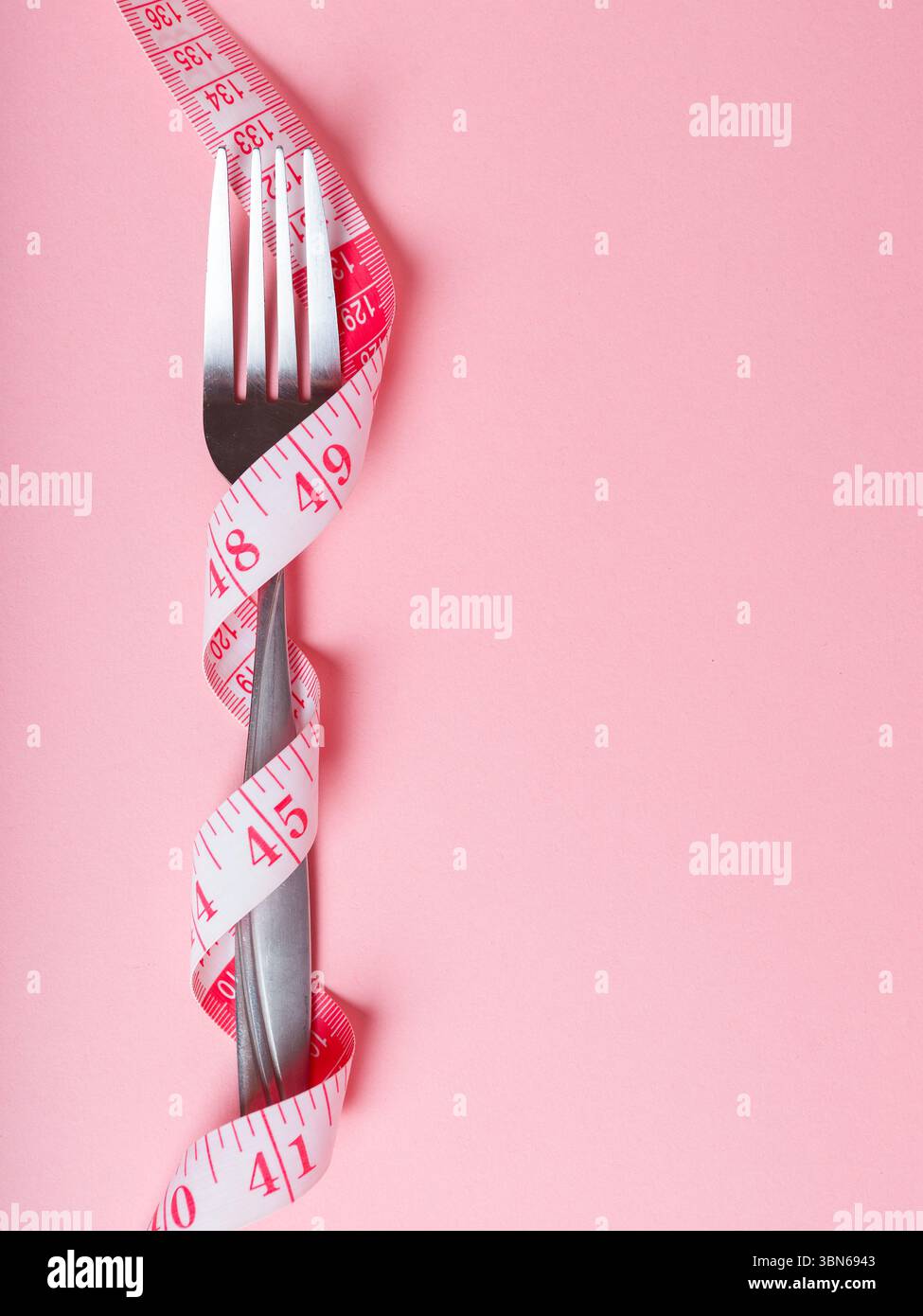 A fork is wrapped with a pink measuring tape on a pink background ...