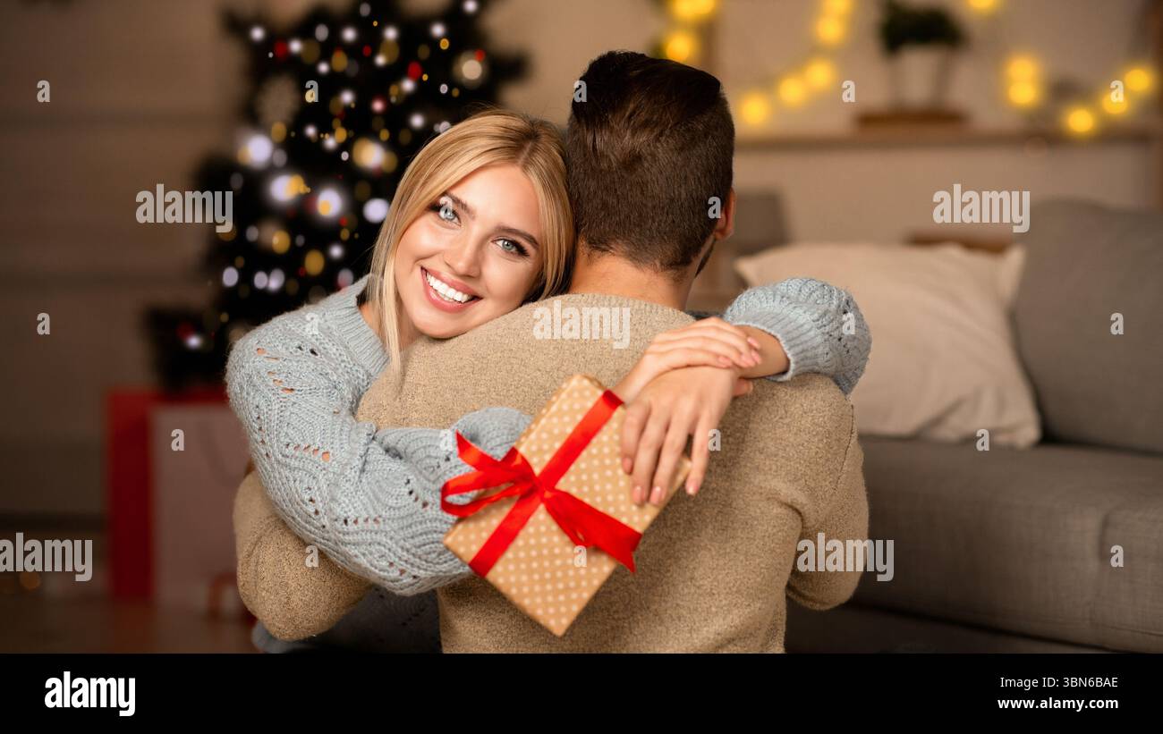 Delighted wife holding xmas gift and hugging her husband Stock Photo ...