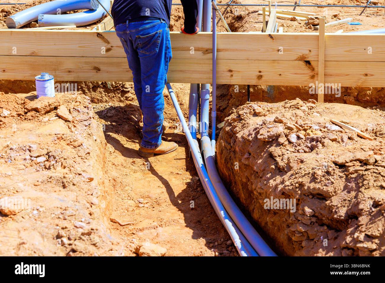 Male worker on installing grey electrical conduits at construction site surrounded by wooden ...