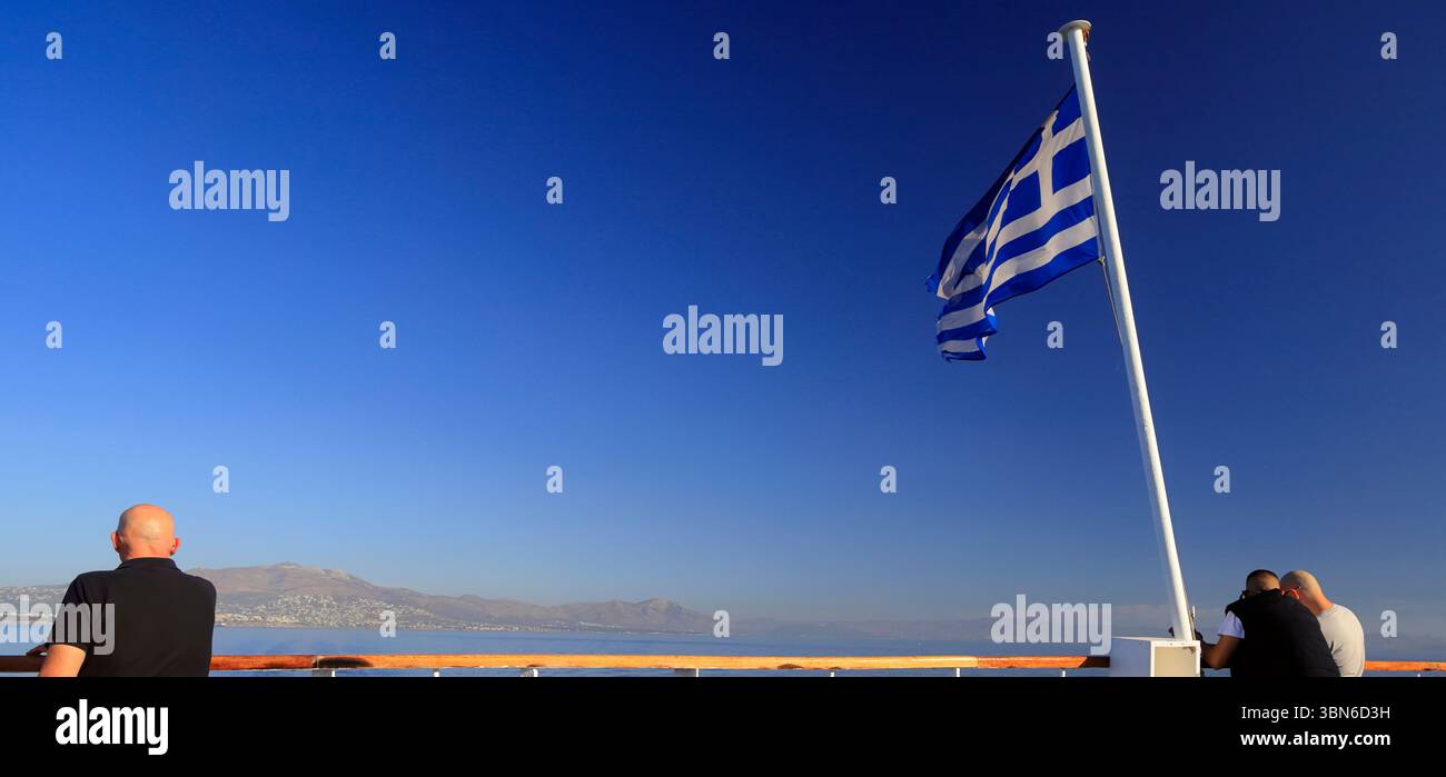 Passengers on a ferry boat looking back to land. Greek flag flying ...