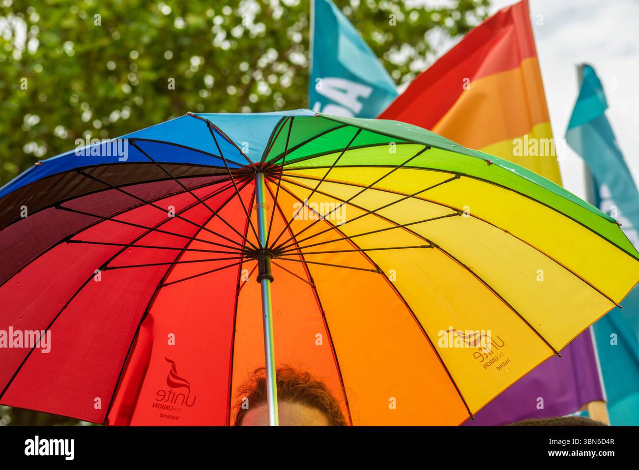 A smiling redhead woman walking out under rain with a rainbow umbrella ...