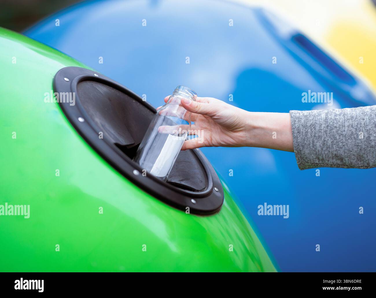 Hand throwing empty glass bottle into yellow recycle bin container outdoors Stock Photo - Alamy