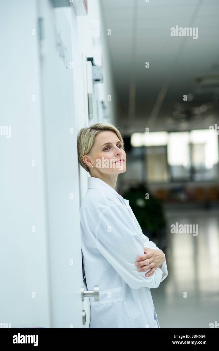 Tired female doctor leaning against wall in hospital hallway Stock ...