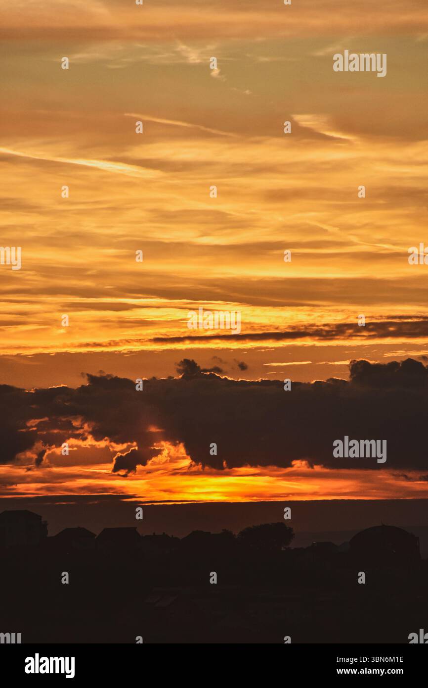 Glowing clouds reflect the setting sun over a silhouetted city skyline ...