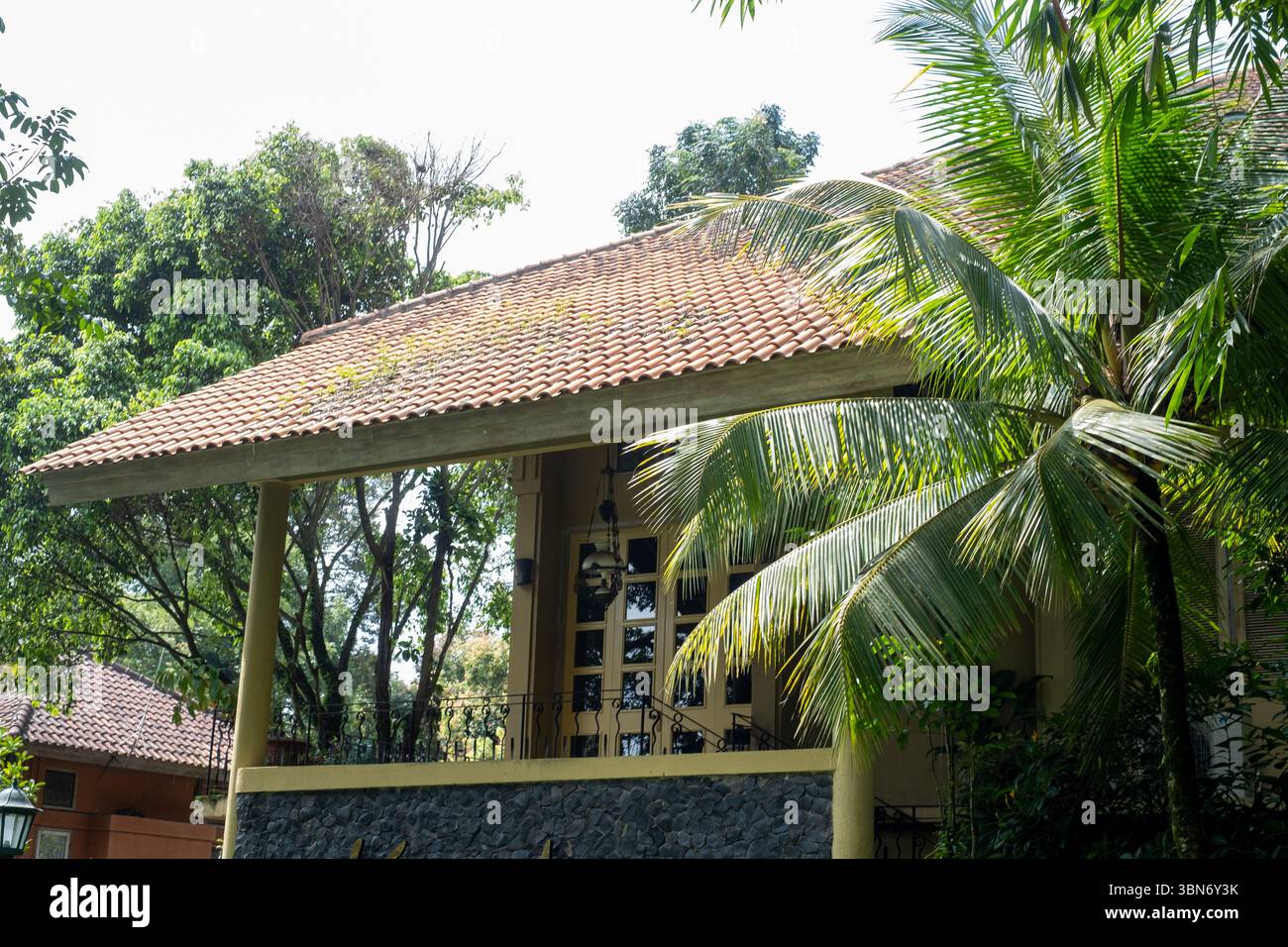 A villa's facade emerges from lush foliage, its tiled roof aged with ...