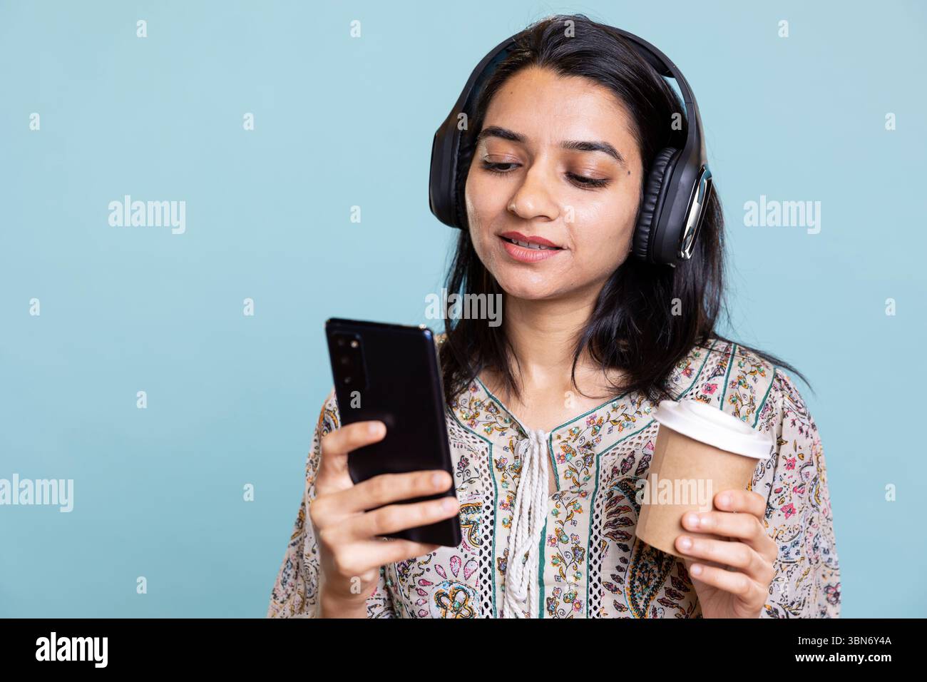 Pleased excited woman playing music on phone and drinking coffee ...