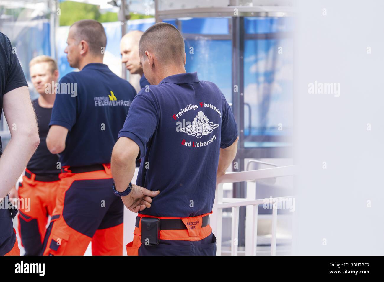 Firefighters in blue and orange uniforms stand together and talk, Fire ...