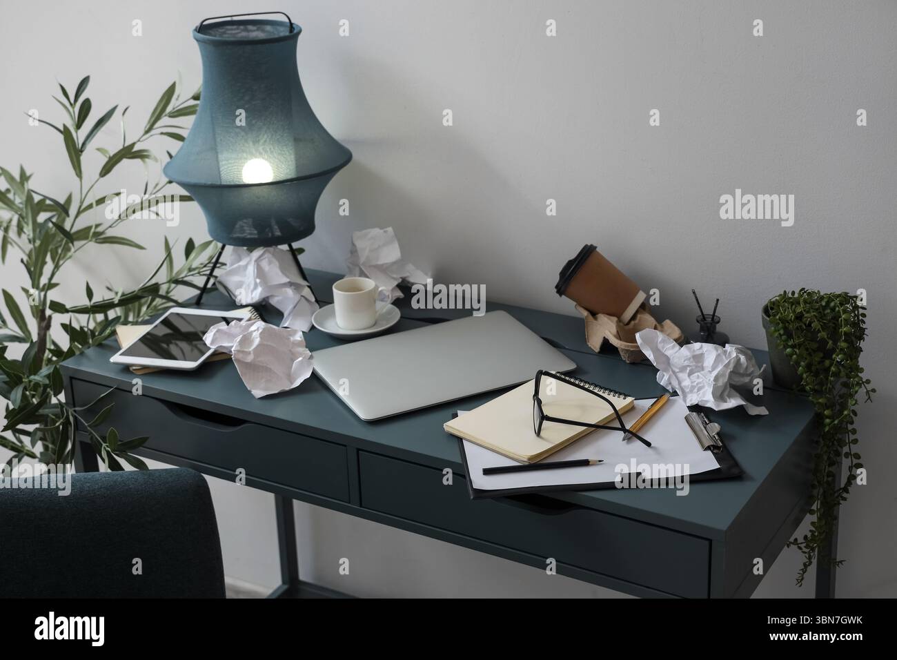 Messy workplace with modern laptop, lamp and papers in light office ...