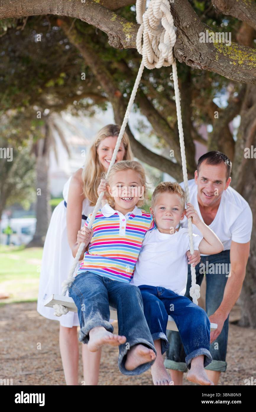 Happy parents pushing their children on a swing Stock Photo - Alamy