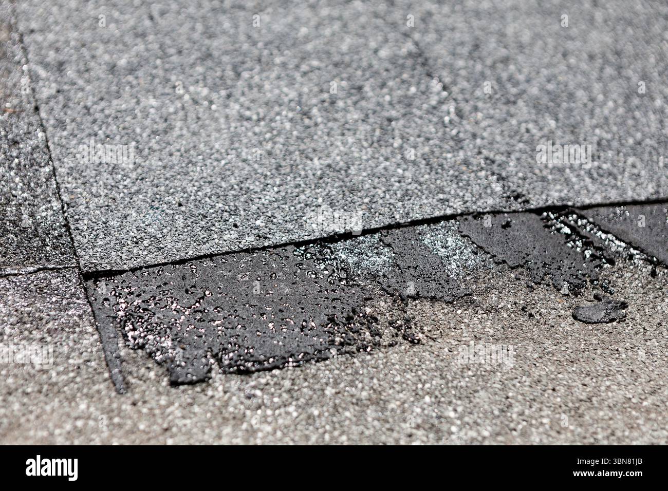 Dark asphalt patch applied to light gray roofing material. Worn patch ...