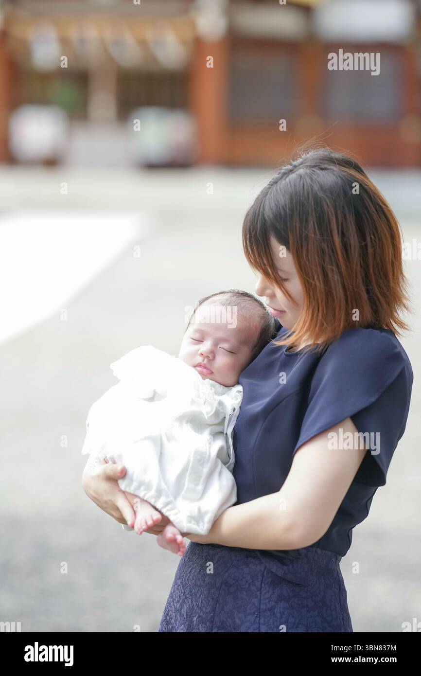 In June 2025, a young Japanese mother in her early twenties gently holds her one-month-old baby ...
