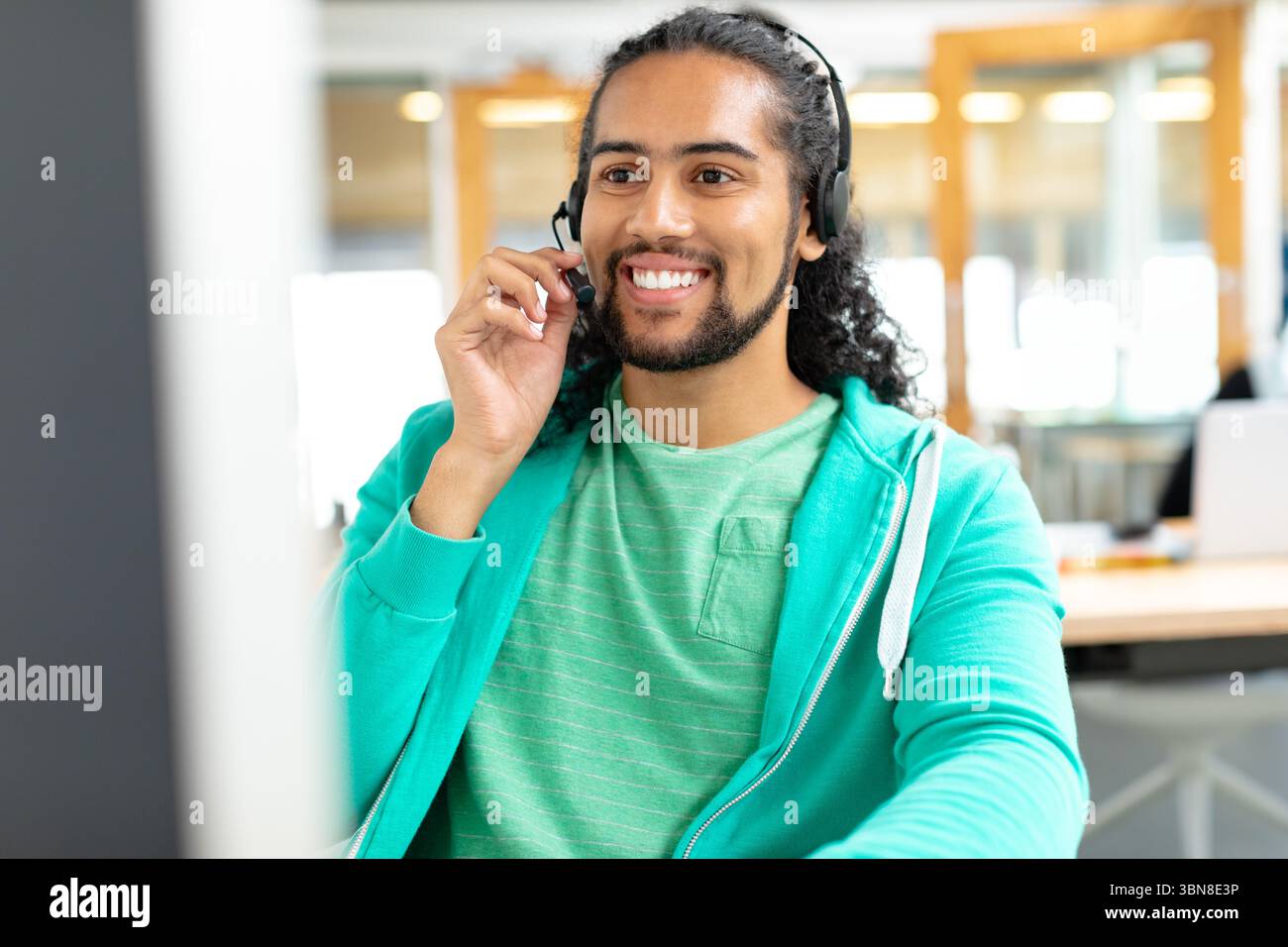 Man speaking into headset with mic at open-plan office desk, viewing ...