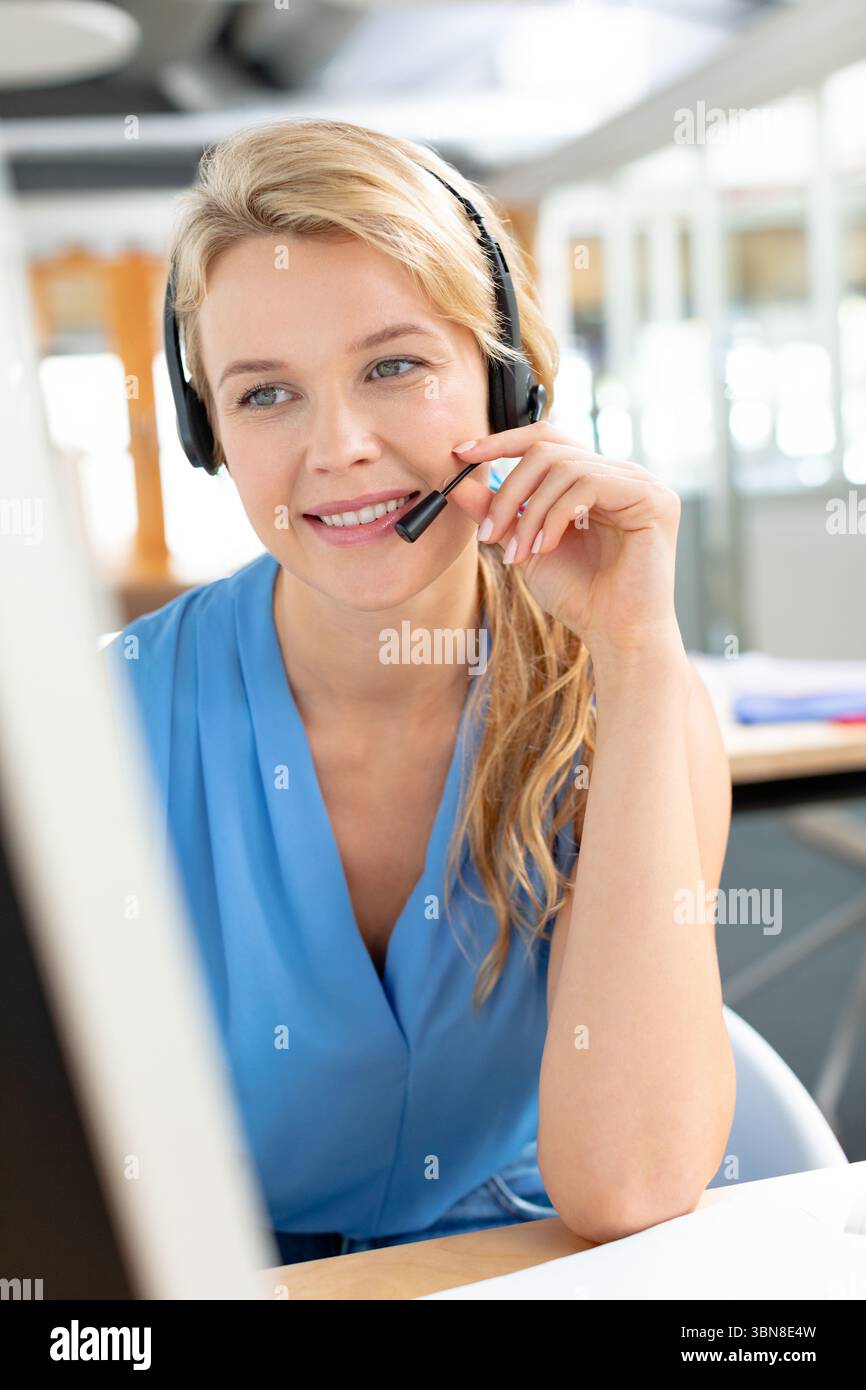 Female call center representative handling calls at desk in open-plan ...
