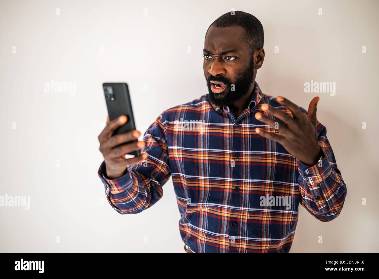 Angry black man in cozy shirt standing in front of wall and having ...