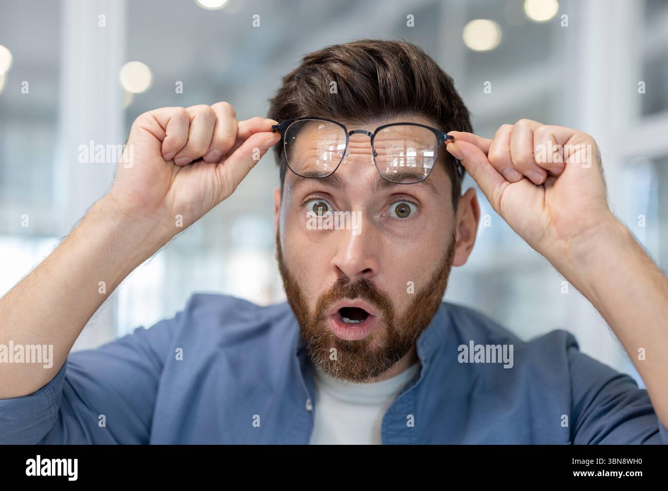 A man with glasses is surprised, holding his glasses with a look of ...
