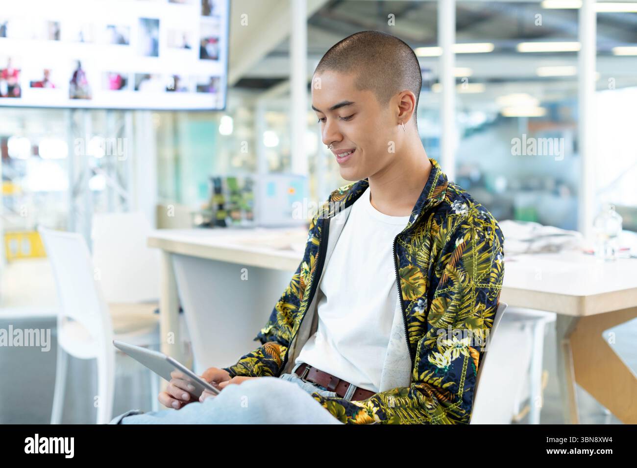 Asian man sitting on white chair at light wood desk in open plan office ...