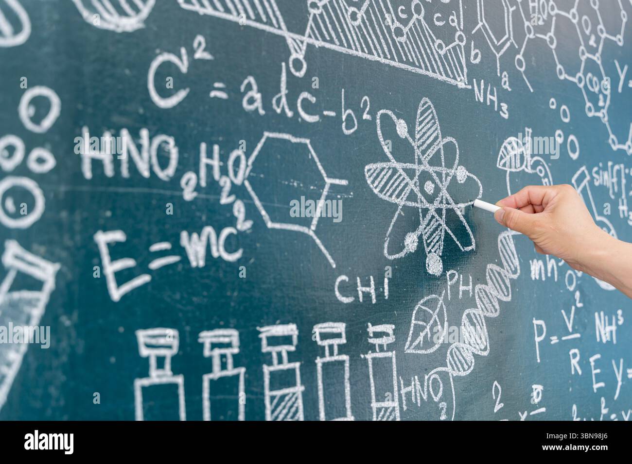Close-up of hand writing chemical formulas and atomic structure using chalk on blackboard ...