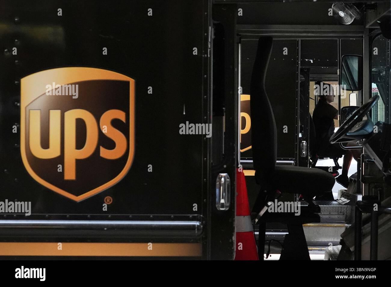 A UPS truck driver makes a delivery and another UPS truck parks in ...