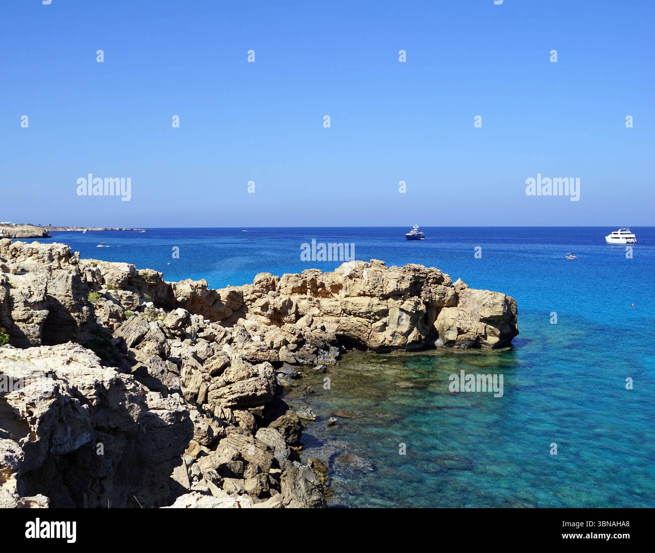 The image depicts a rocky coastline with a clear blue sky and a deep ...