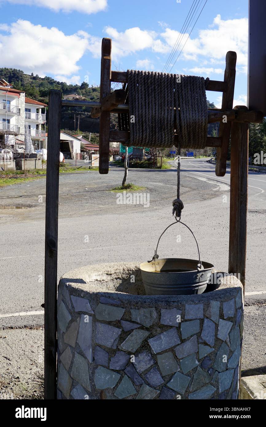 A rustic wooden well with a metal bucket hanging from a rope. The well ...