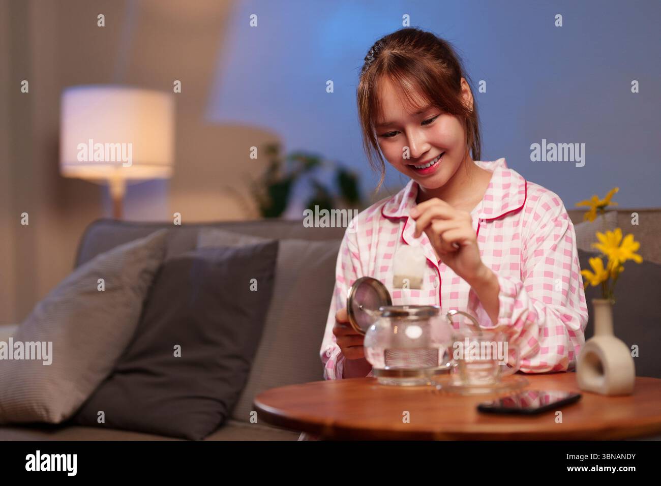 This image shows an Asian adult woman making tea in her cozy home to ...