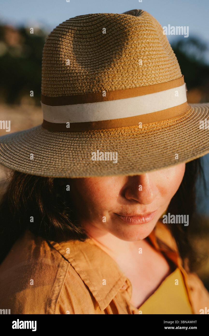 Close-up of a woman with a straw hat shaded over her face, casting soft ...